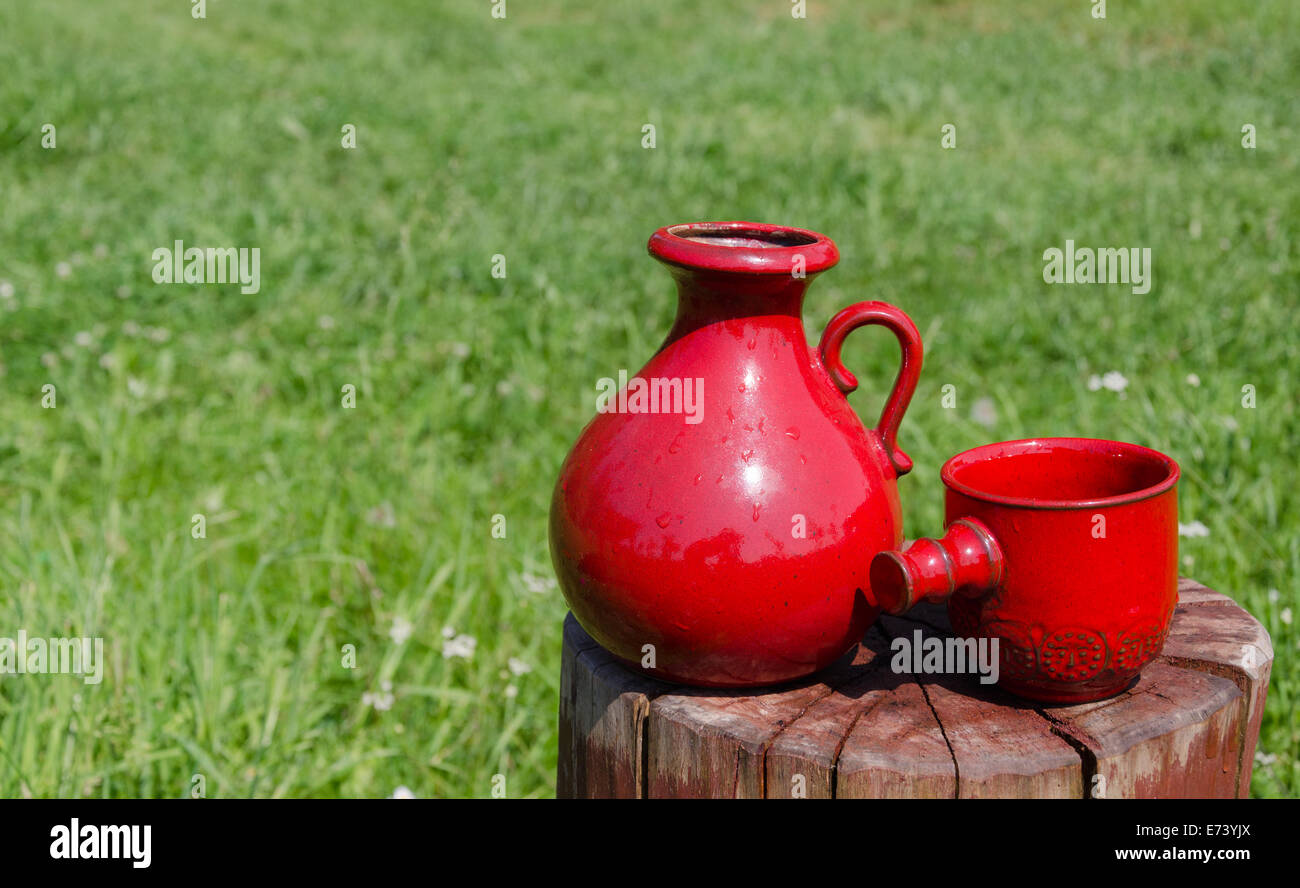 close up of two ceramic red water jug and cup on stump nature ...
