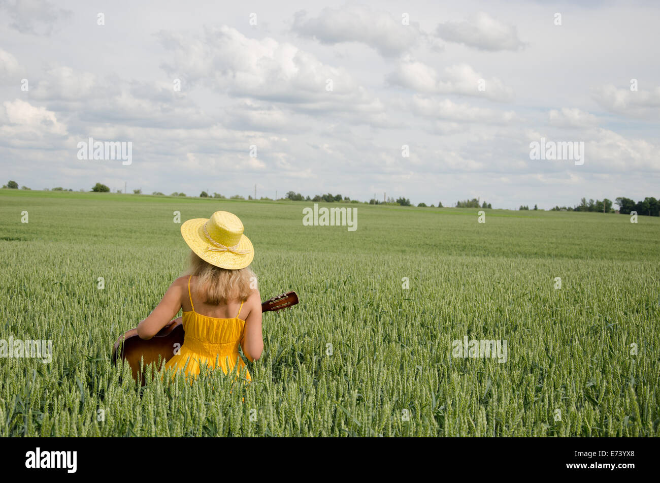 Country woman in yellow dress and hat on head play with guitar at wheat ...