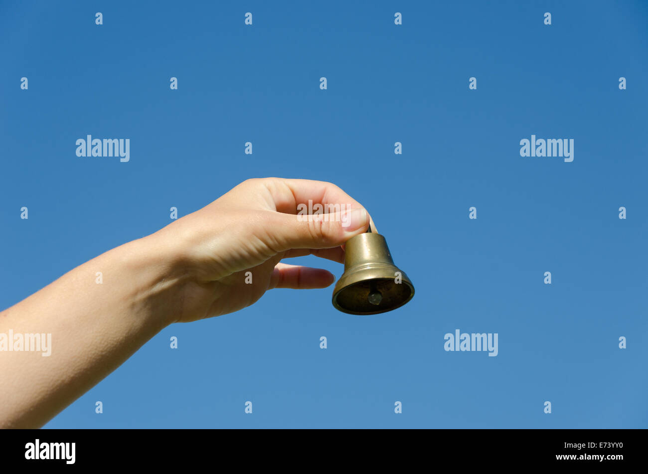 female hand hold small brass old jingle on blue sky background Stock ...