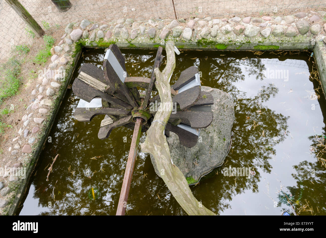 stylized small wooden water mill on the stone base of the park pond ...