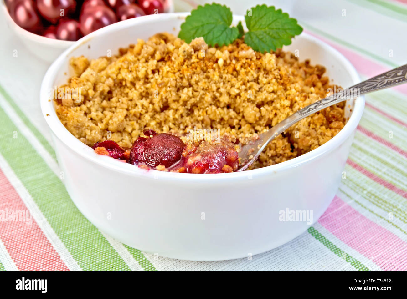 Cherry crumble in a white bowl with a spoon, cherries on a background ...