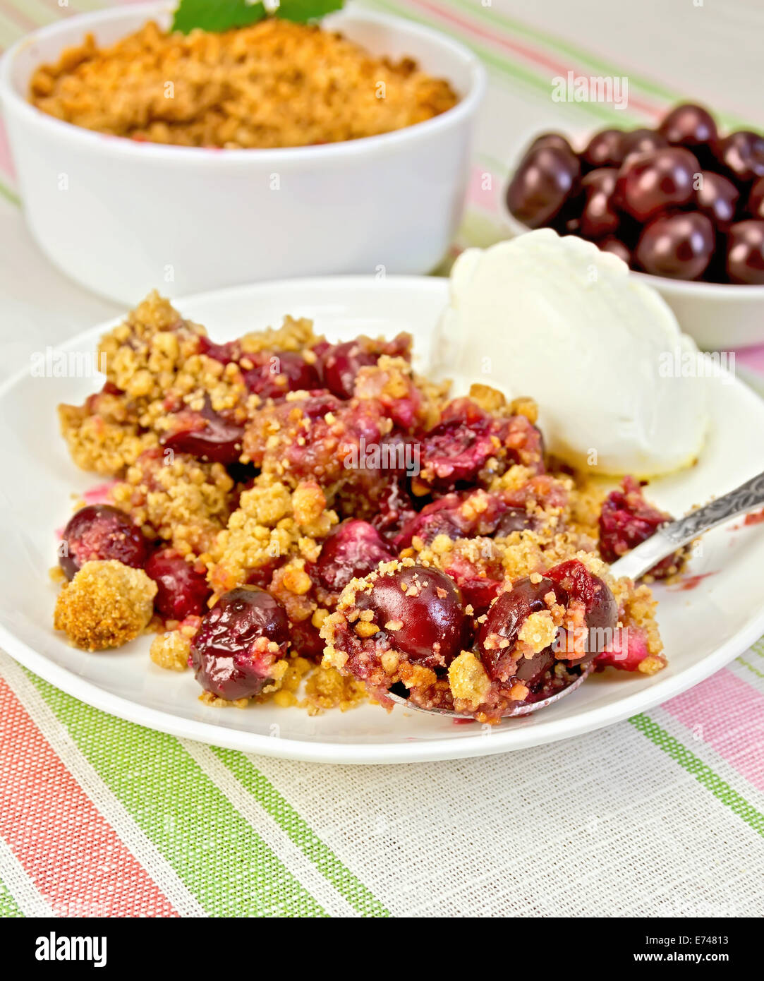 Cherry crumble in a white bowl and a plate with a spoon, cherries on a ...