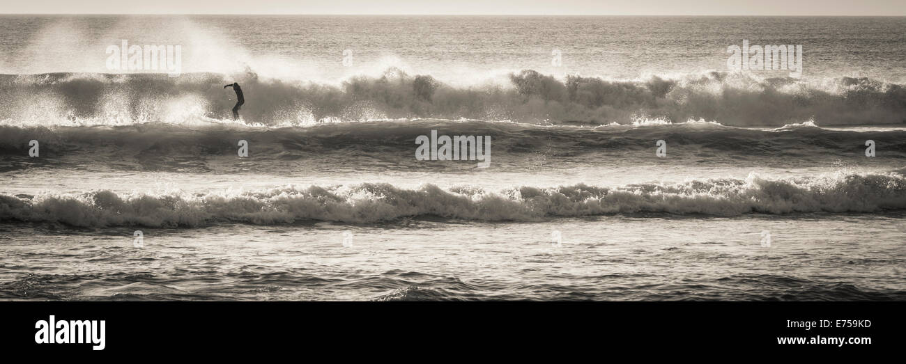 Surfer riding a long wave with spray rising up from the ocean Stock ...