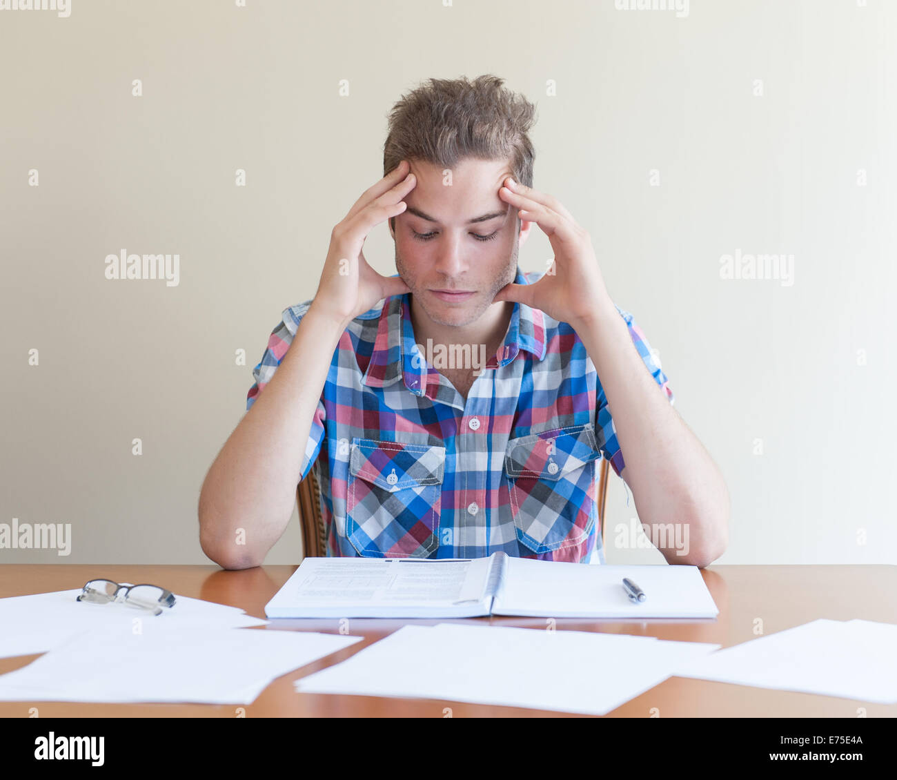 Young adult studying ,feeling frustrated, in a messy desktop. paper ...