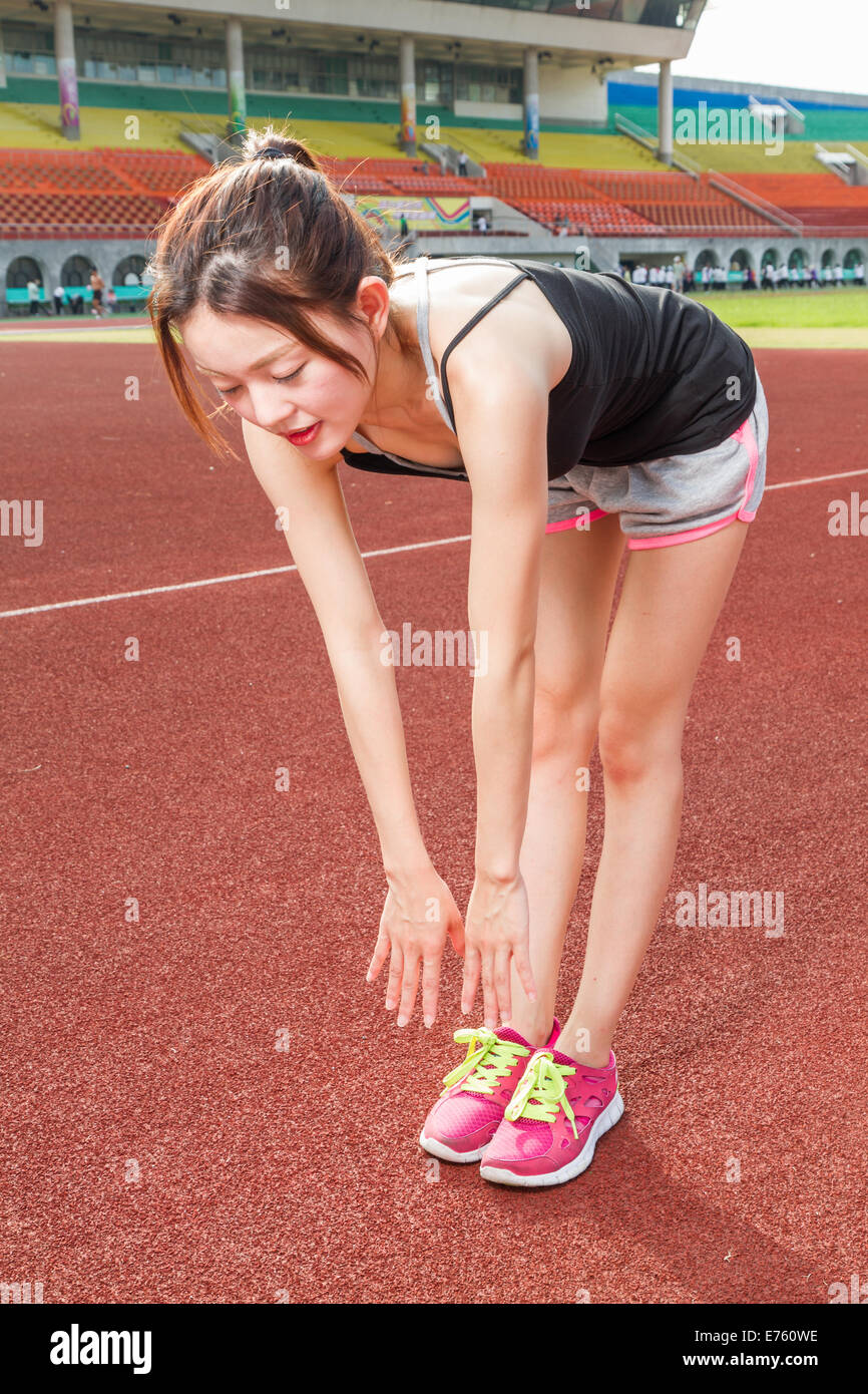 Asian Chinese Woman Stretching Before Exercise On Track At Stadium