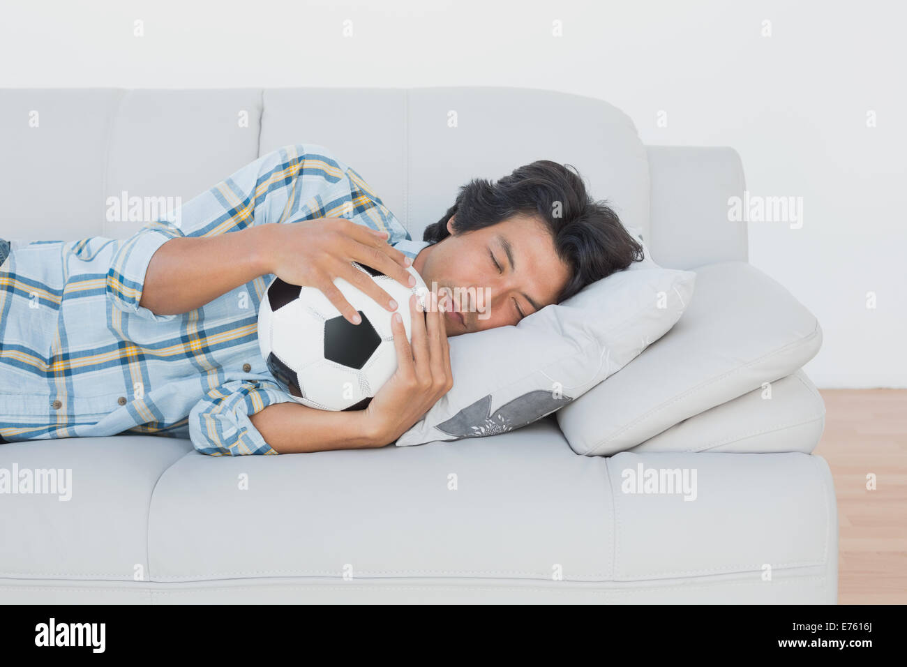 Football fan hugging ball on couch Stock Photo - Alamy