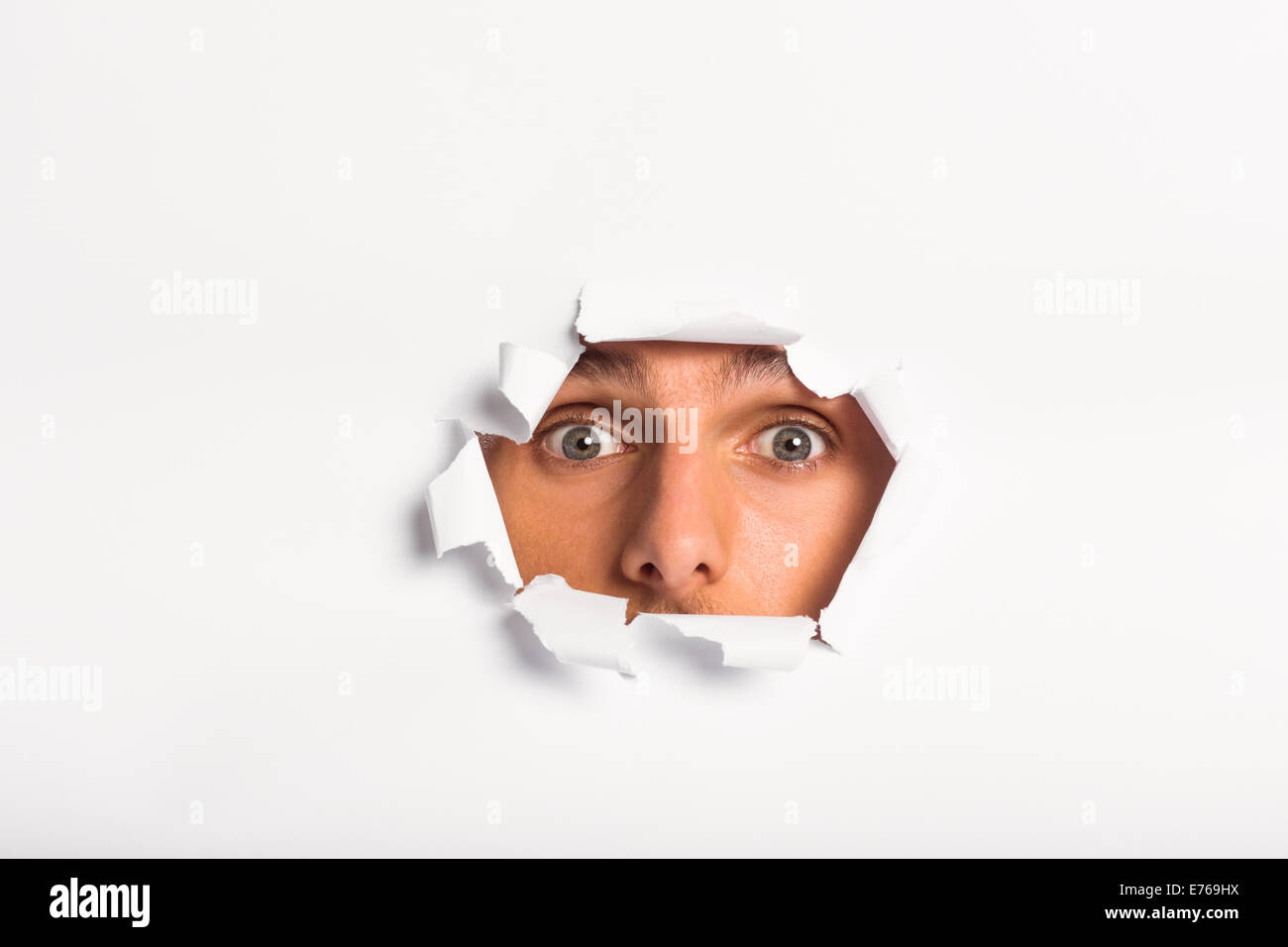 Young man looking through paper rip Stock Photo - Alamy