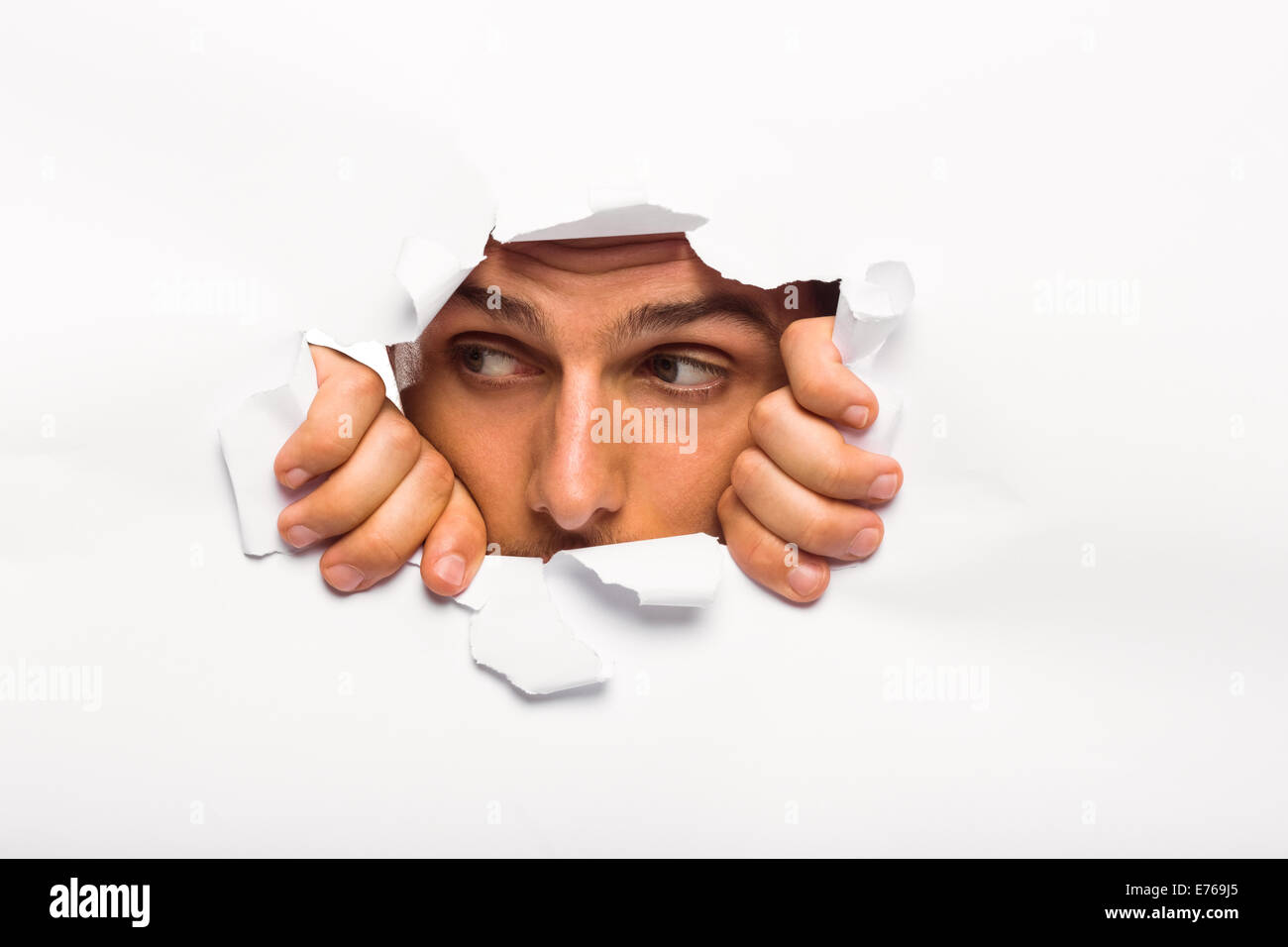Young man looking through paper rip Stock Photo - Alamy