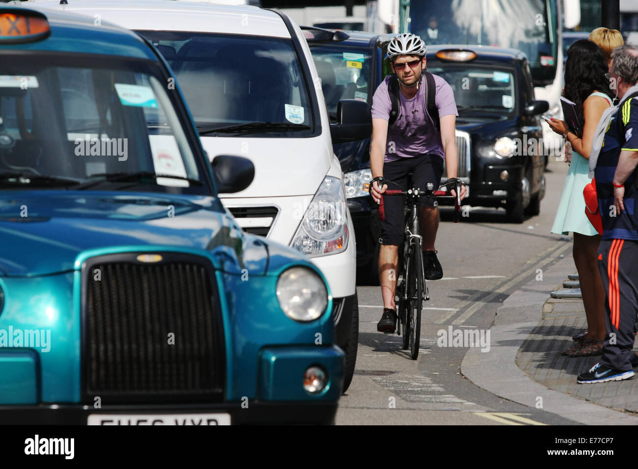 A cyclist cycling in London amongst a queue of traffic. Pedestrians ...