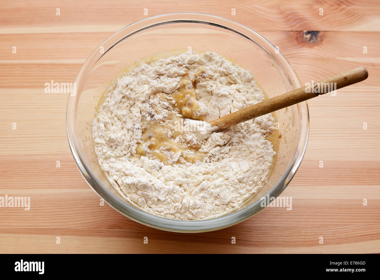 Flour being stirred into wet batter for banana loaf, in a glass bowl on ...