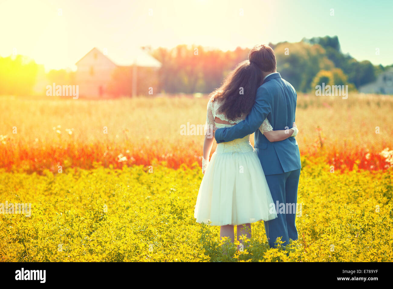 Young happy wedding couple hugging in the meadow back to camera and ...