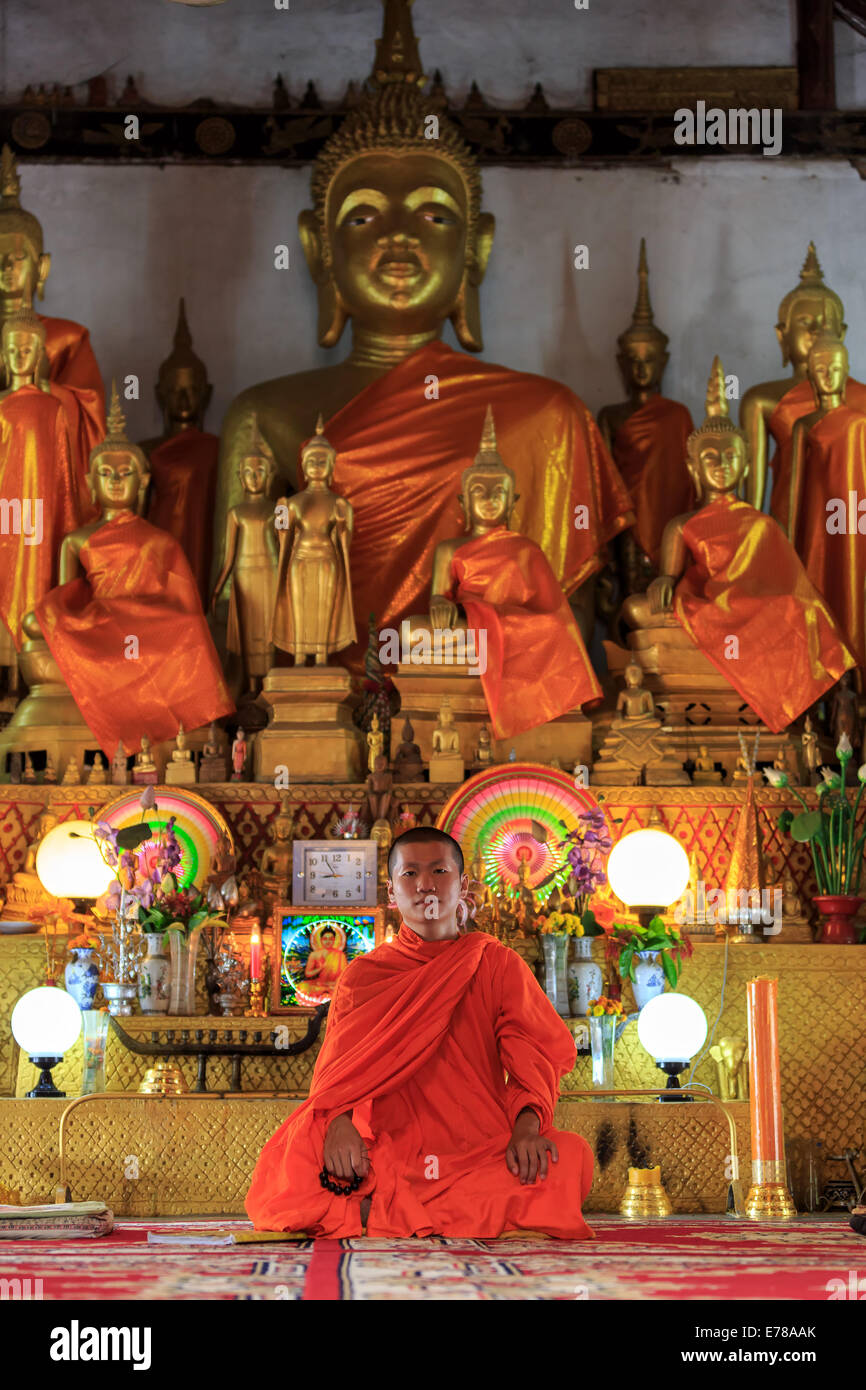 A monk meditating in the lotus position in front of golden Buddhas ...