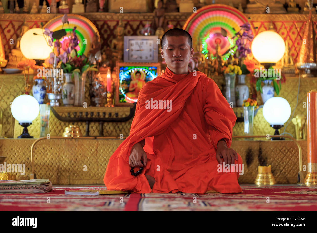 A monk meditating in the lotus position in front of golden Buddhas ...