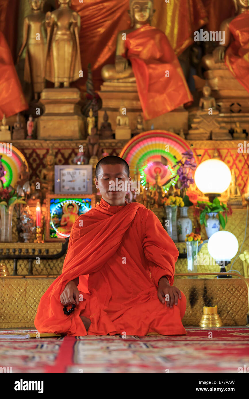 A monk meditating in the lotus position in front of golden Buddhas ...