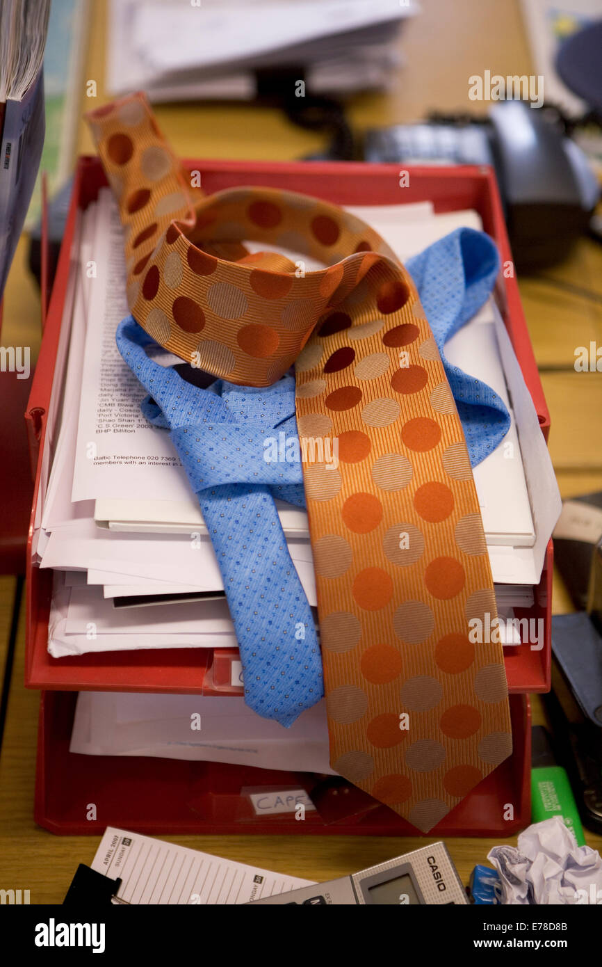 Two brightly colored ties lie in the out tray of messy office desk ...