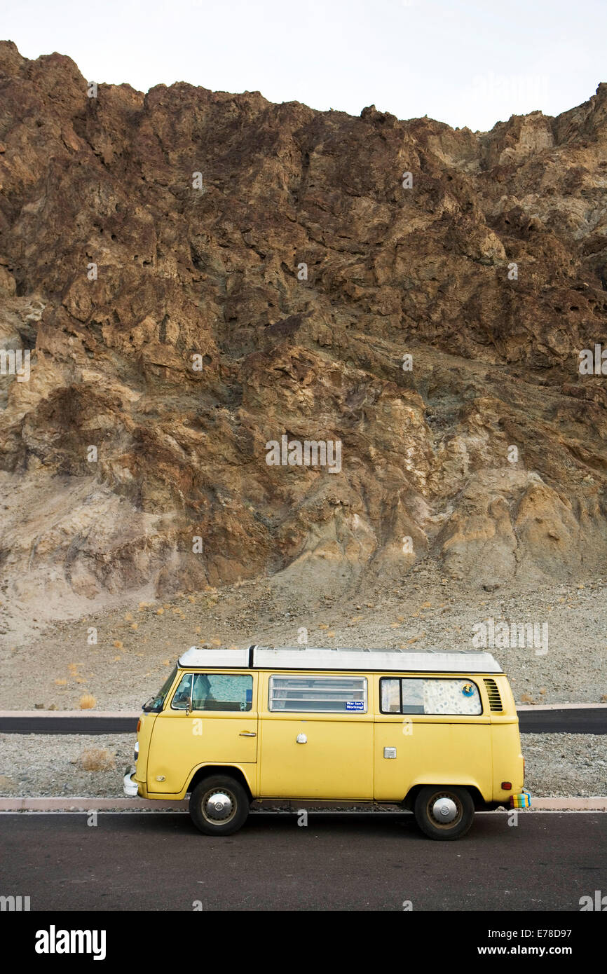 A classic yellow campervan is parked on the roadside under a sandy ...
