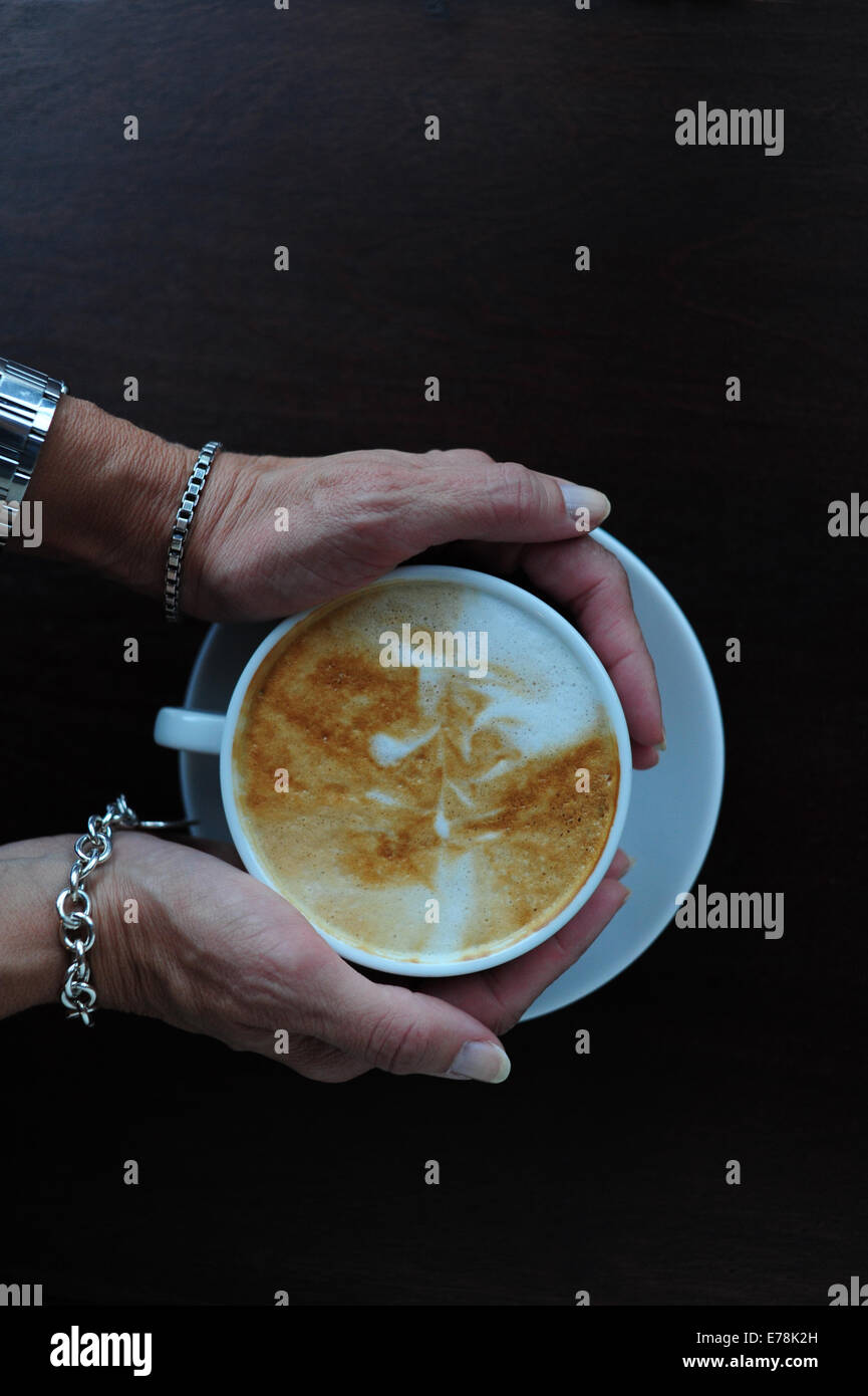 Mature woman in cafe holding a cup of coffee cappuccino over head view ...