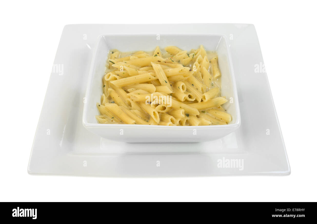 A square bowl of cooked pasta in a thick cream sauce with parsley and ...