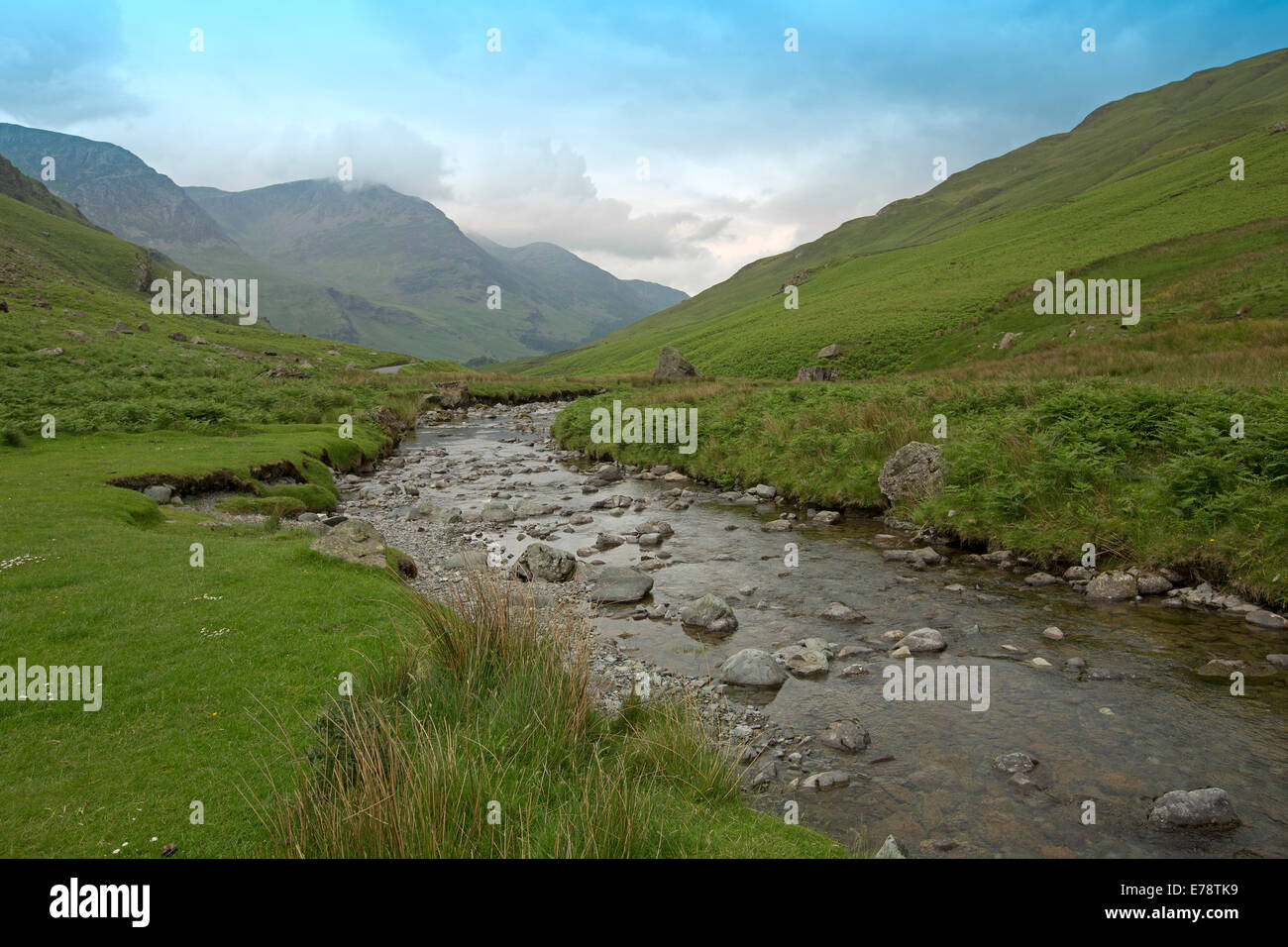 Shallow stony stream and vast landscape of green treeless mountains ...