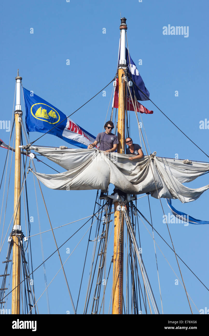 Crew members work high up in the rigging of a tall ship adjusting the ...