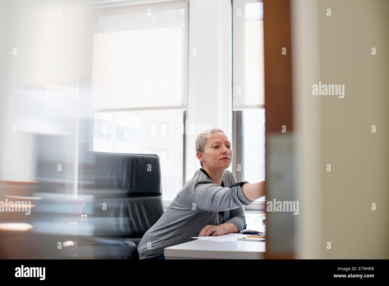 A woman working in an office alone, at her desk leaning forward to look ...