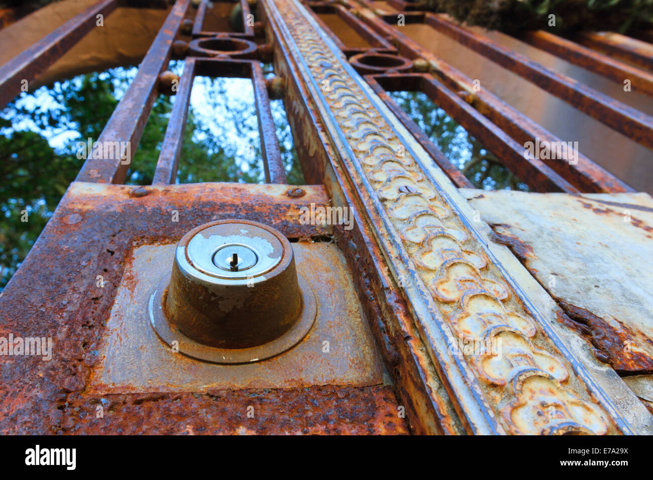 Looking up at ornate rusty iron gate with key lock preventing entry ...