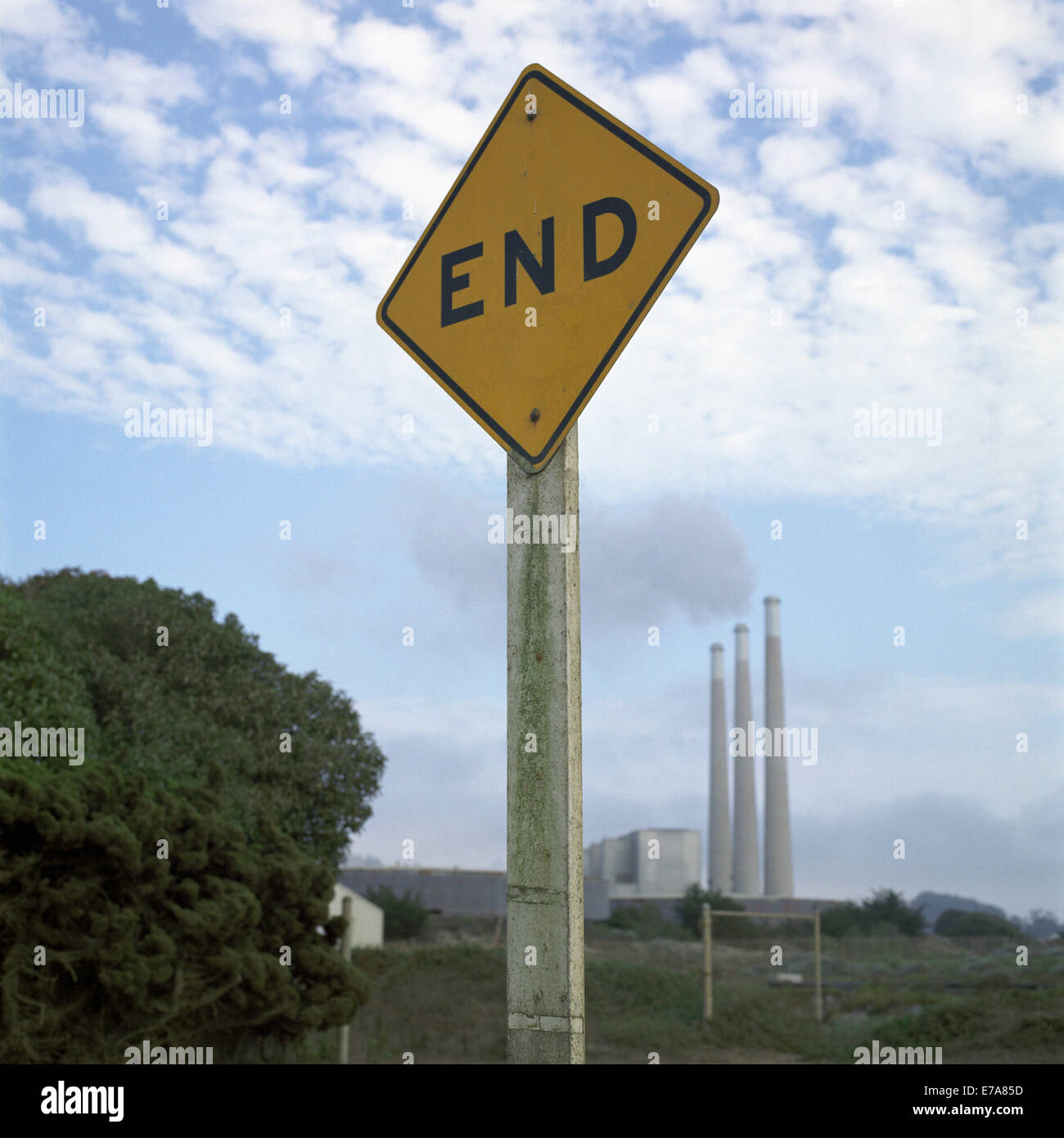 A dead end road sign in foreground, smoke stacks emitting smoke in ...
