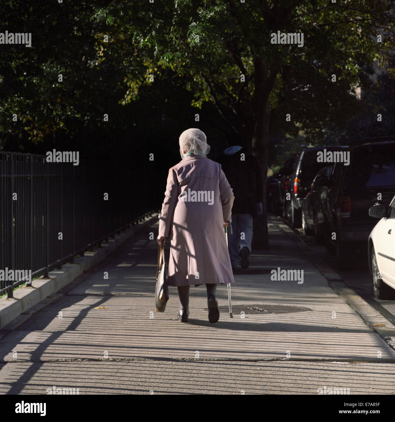 A senior woman using a cane walking on a city sidewalk, rear view Stock ...