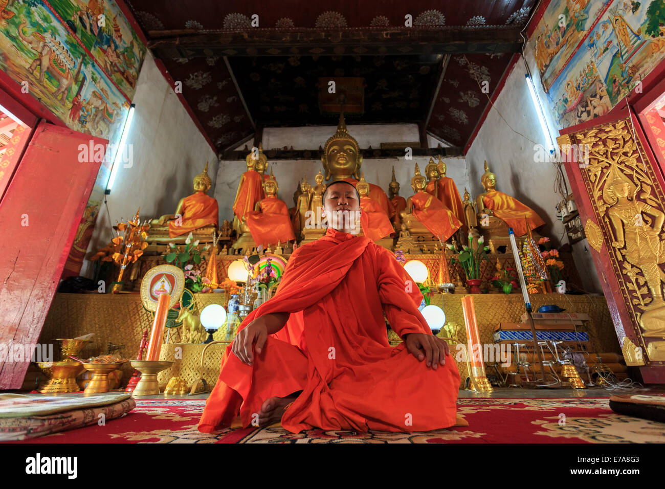 A monk meditating in the lotus position in front of golden Buddhas, low ...