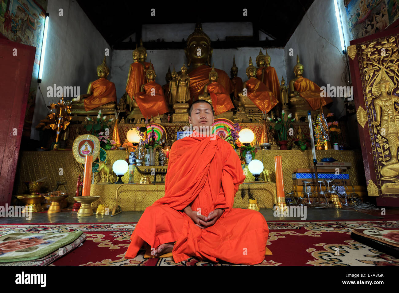 A monk meditating in the lotus position in front of golden Buddhas ...