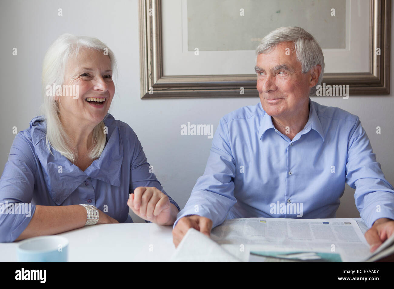 Happy senior couple with newspaper sitting at table in house Stock ...