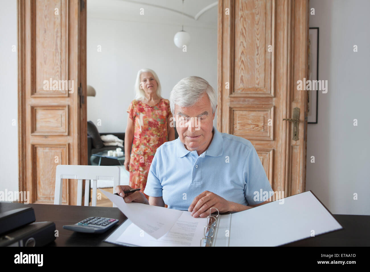 Senior man reviewing financial documents with woman in background at ...