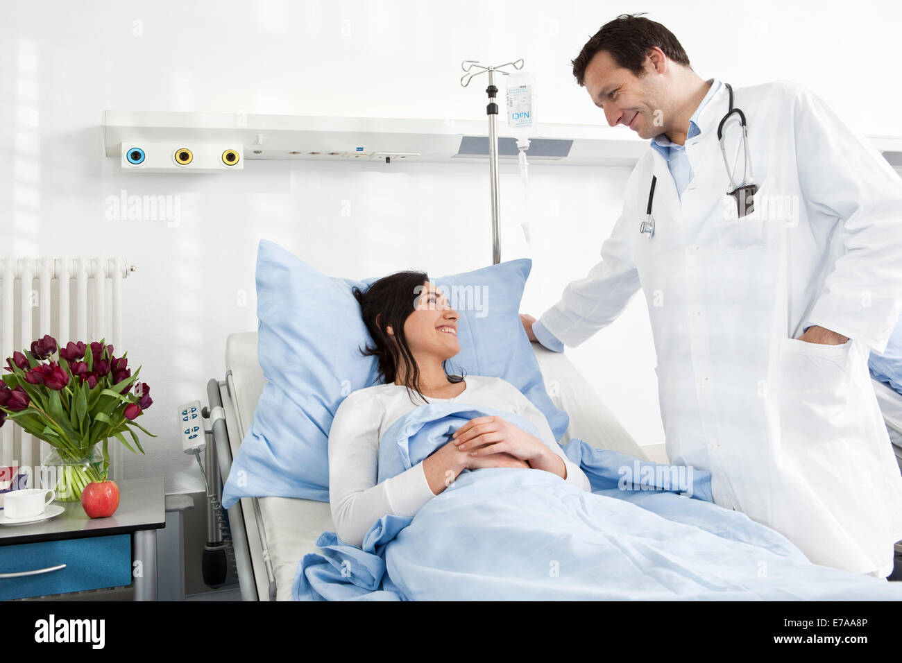 A doctor talking to a smiling patient lying in a hospital bed Stock ...