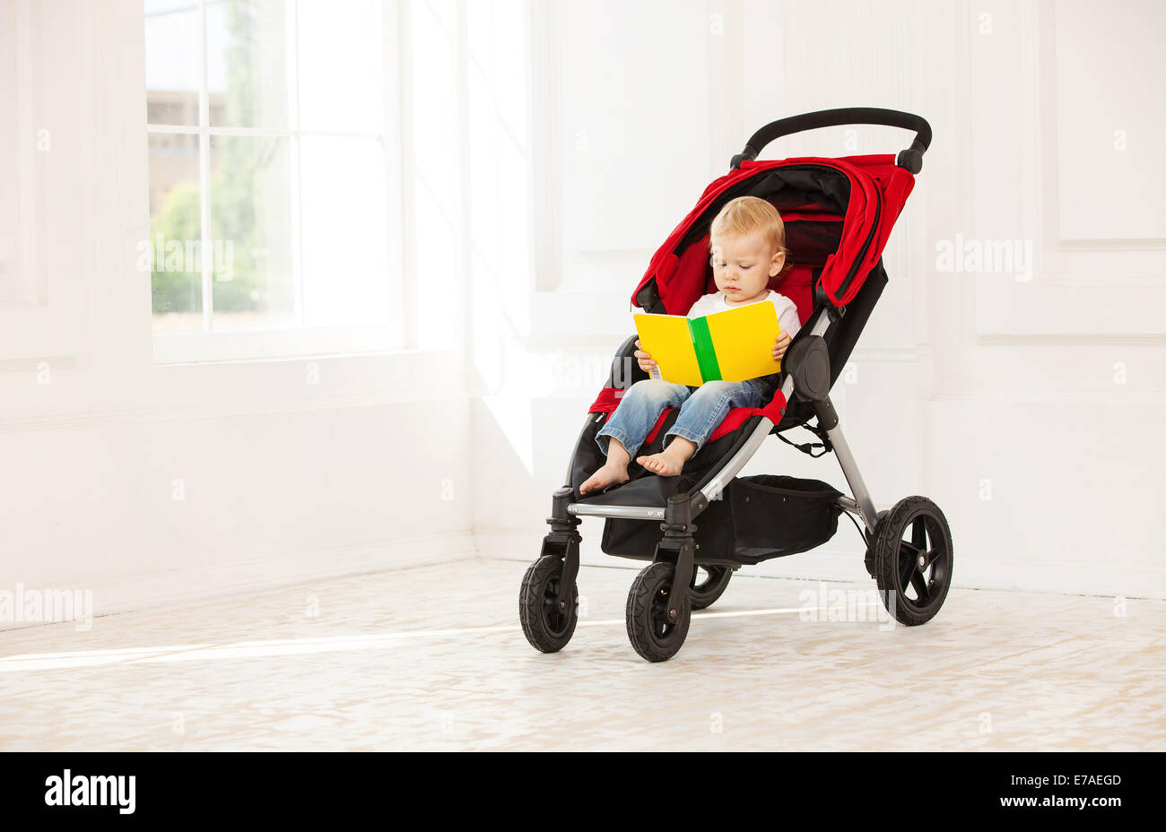 Toddler boy sitting in stroller at home and looking at open book Stock ...