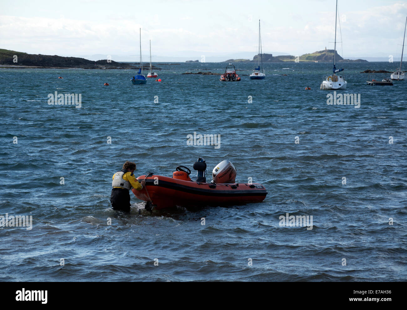 An RNLI volunteer wades into the sea to launch an inflatable lifeboat ...