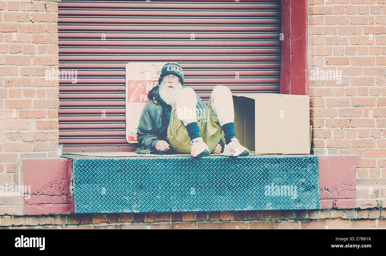 A poor homeless man sits on a truck loading next to his cardboard box ...