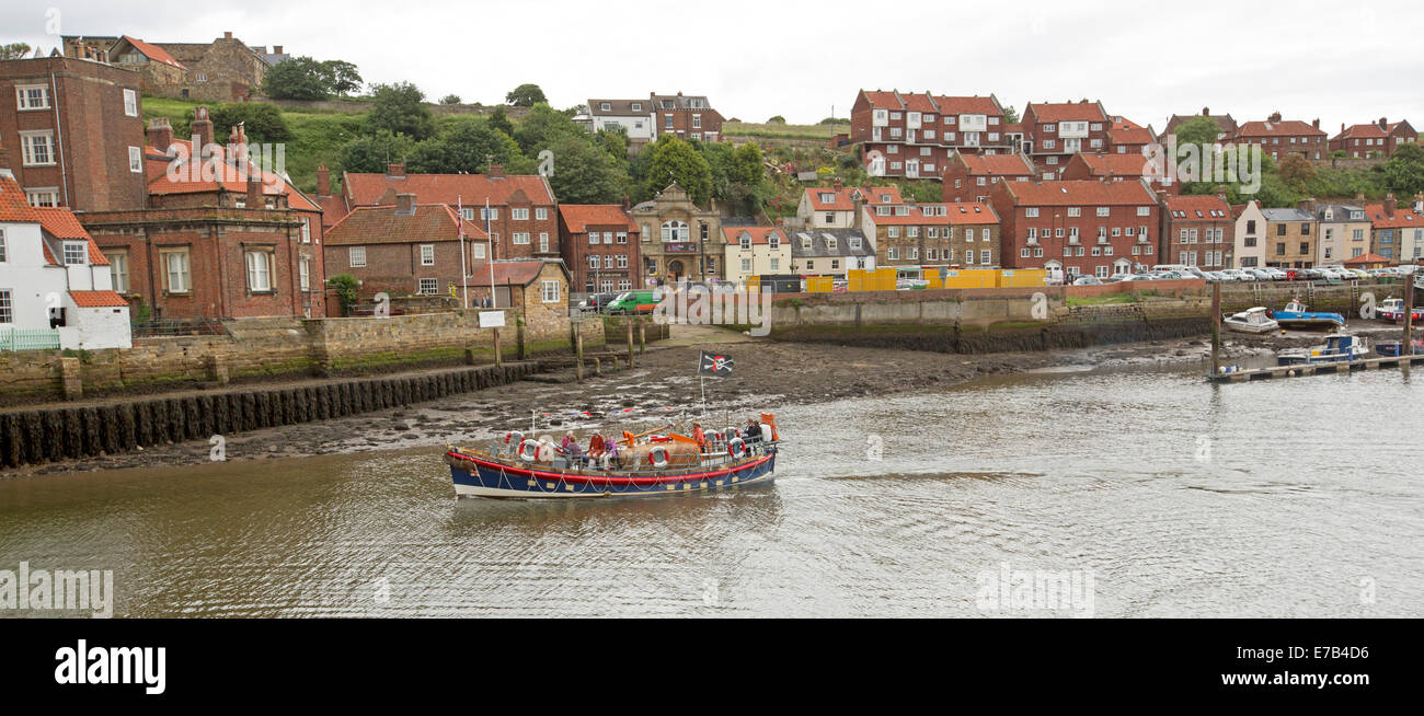 Tour boat cruising through Whitby harbour with buildings of English ...