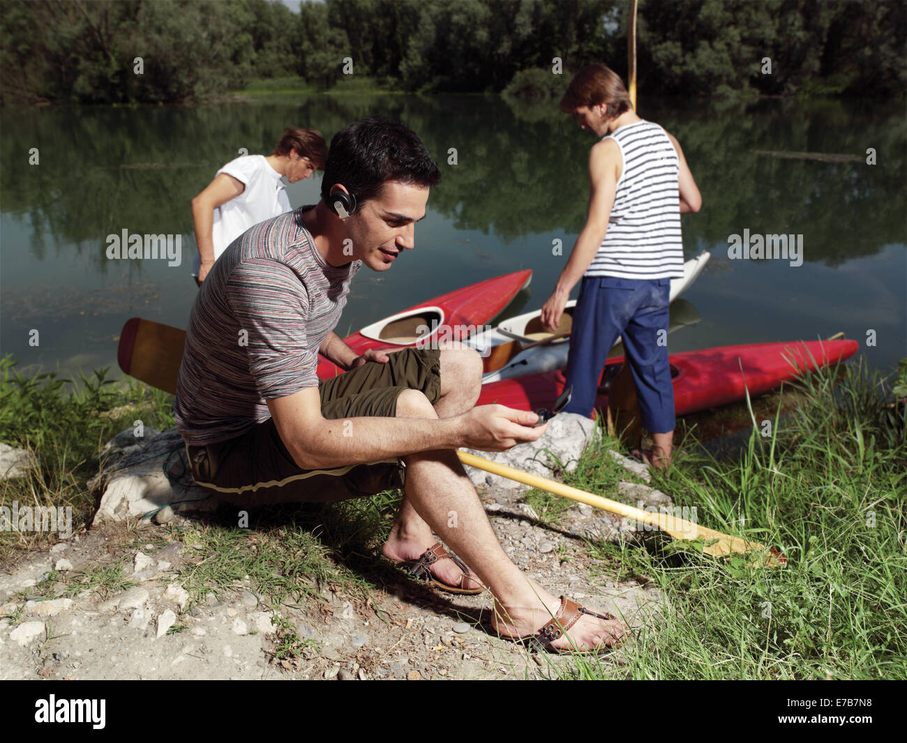Young men with friends near river, discussing how to paddle in a kayak ...