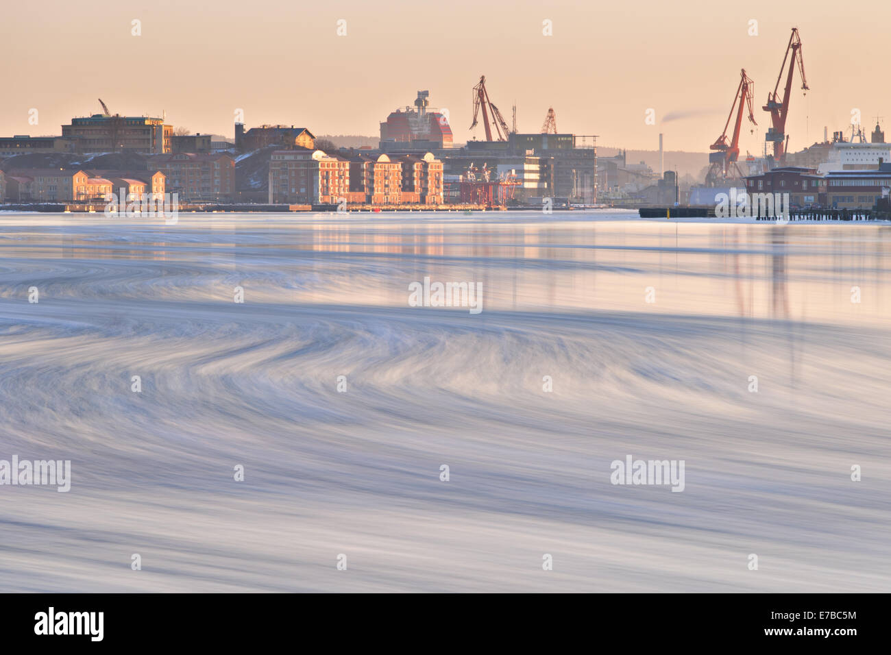 Swirled patterns of snow on a partly frozen river running by a shipyard ...