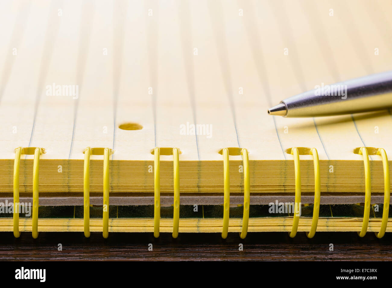 Macro of the spiral of a yellow paper notebook with a metallic pen ...
