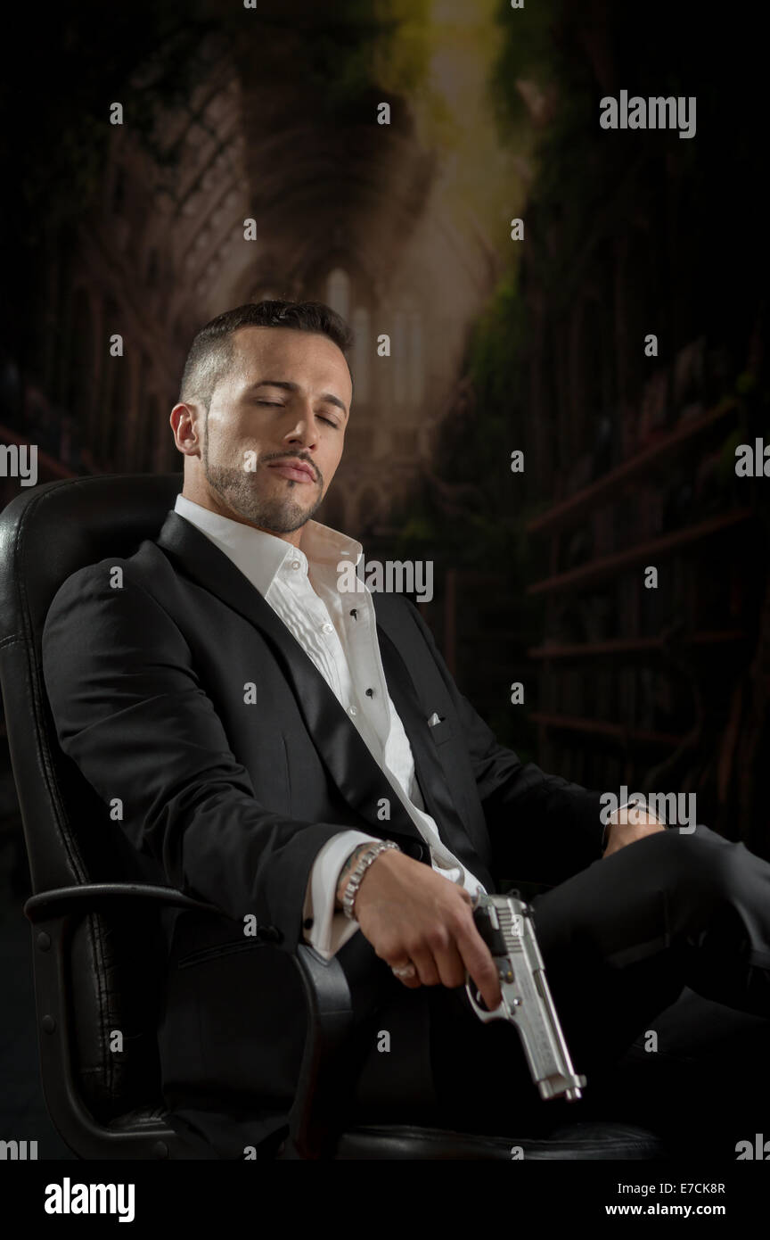 Elegant man sitting in a chair holding gun over dark background Stock ...