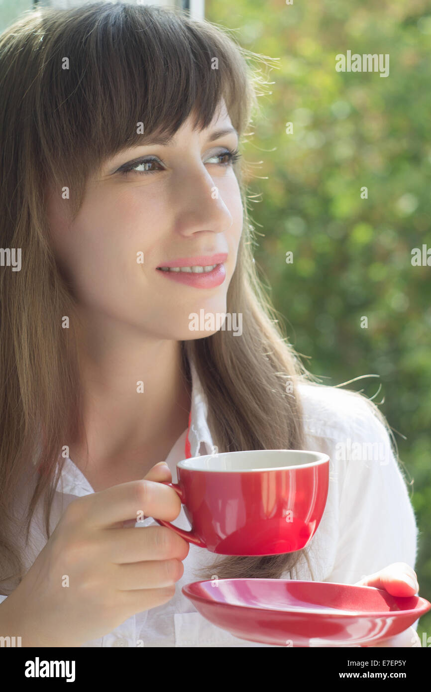 Young adult caucasian girl dreaming near window with cup of tea or ...
