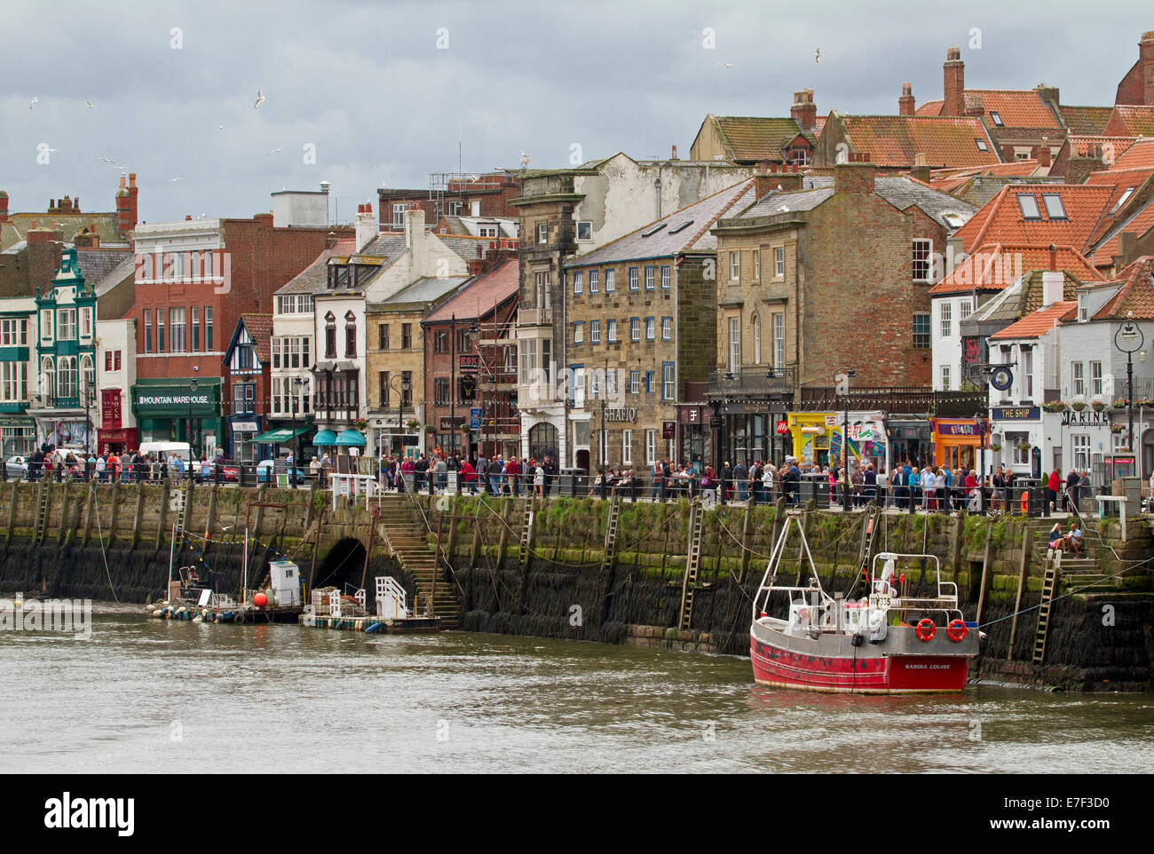 Crowd of people strolling beside Whitby harbour with buildings of ...