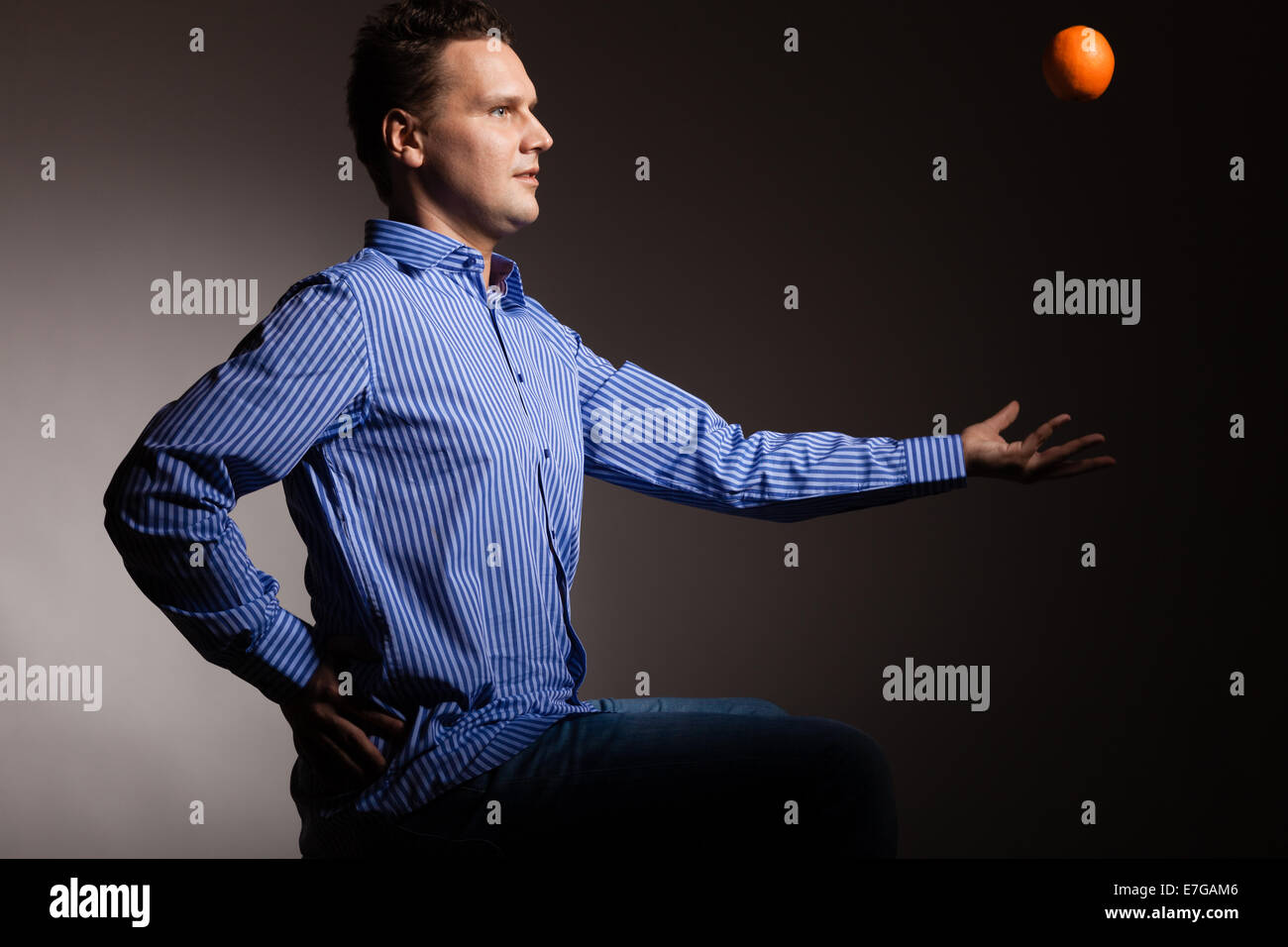 Diet and nutrition. Young smiling man throwing orange tropical fruit on ...