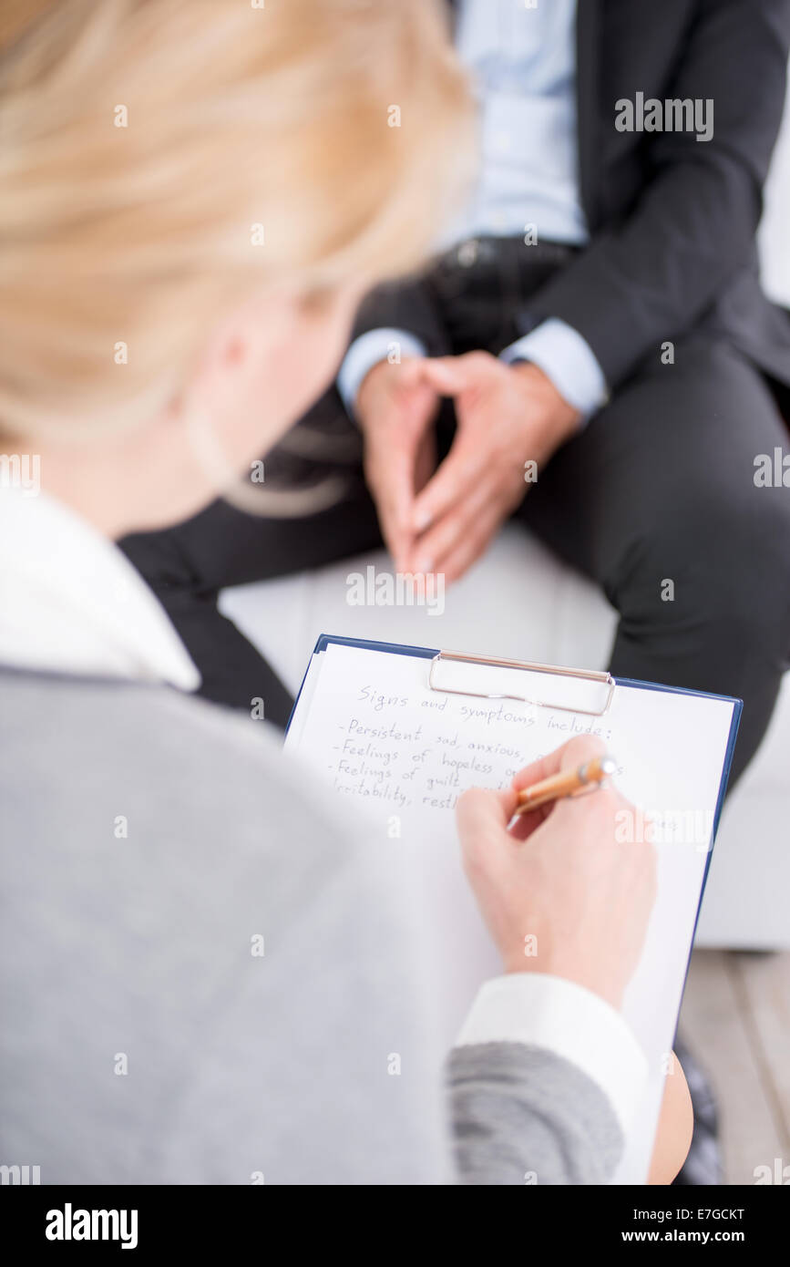 Female psychologist making notes during psychological therapy session ...