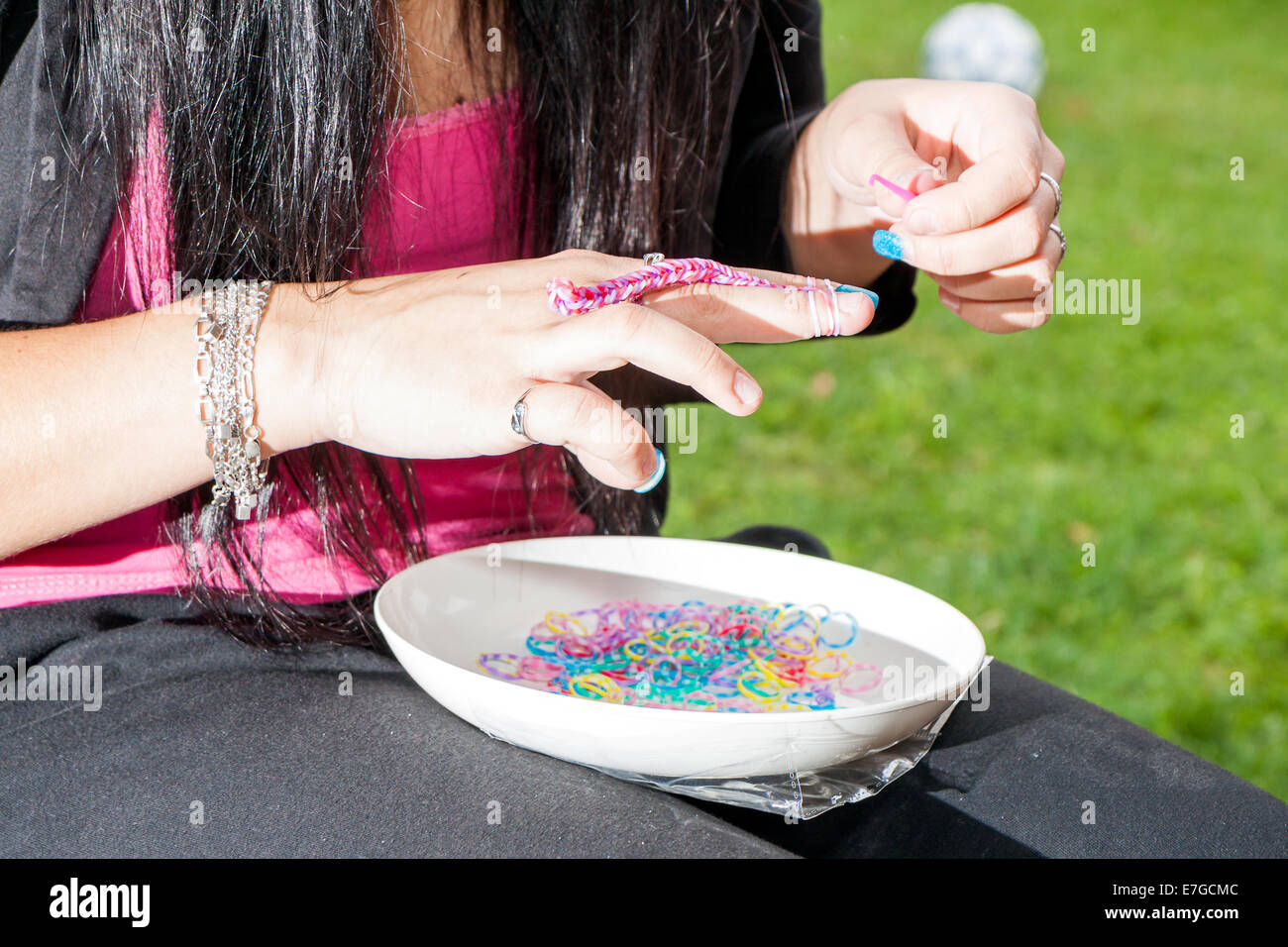 Girl with colorful nails making a rubber loom bracelet with a hook ...