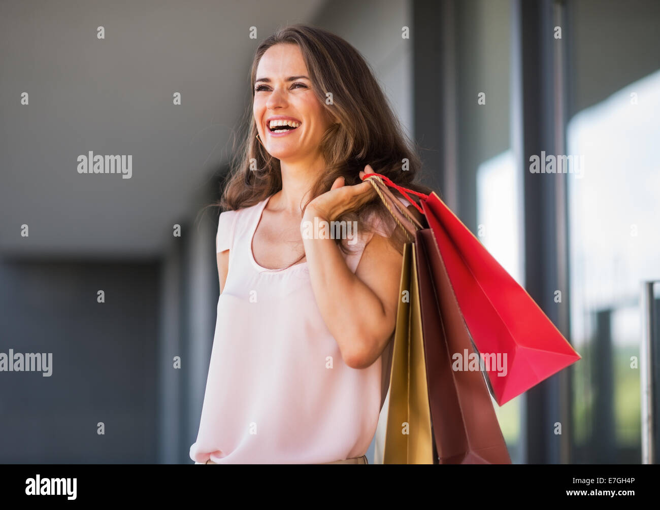 Portrait of smiling young woman with shopping bags on the mall alley ...
