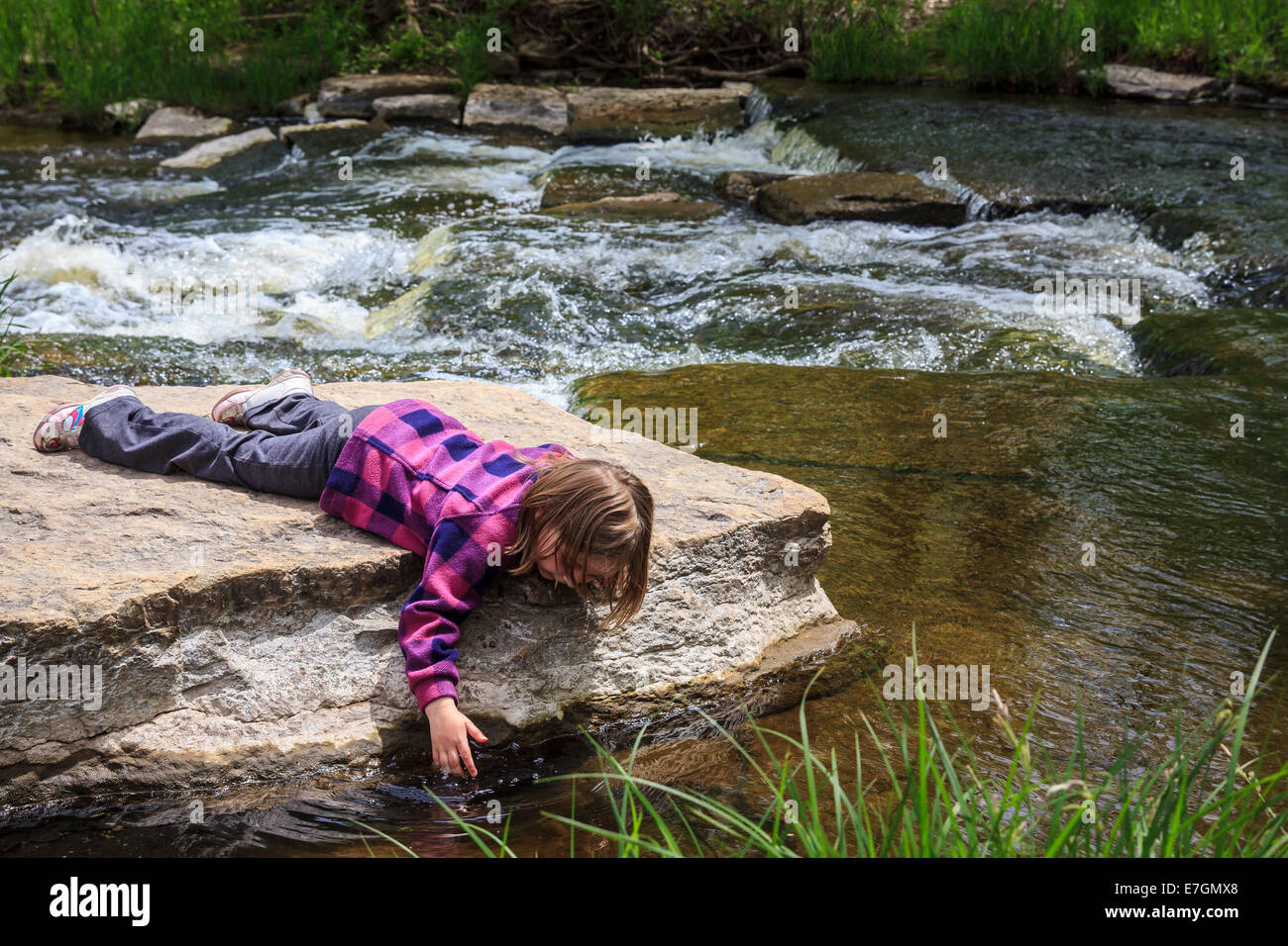 Young girl playing by a stream in the woods. Tentatively dipping her ...
