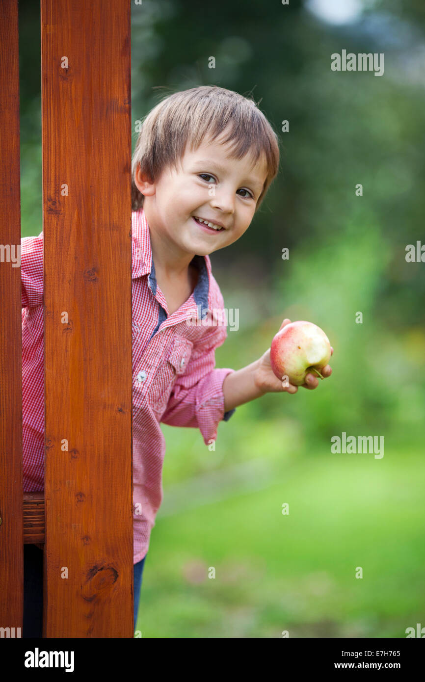 Adorable boy, holding apple, standing next to wooden door Stock Photo ...