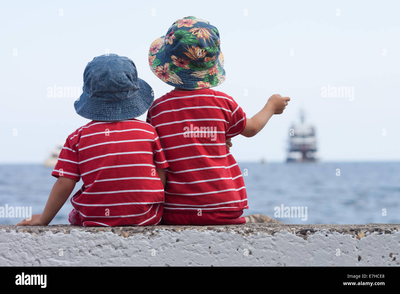 Two boys, contemplating a big ship in the sea, sitting on a wall Stock ...